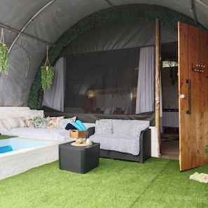 Uma tenda com um sofá, uma mesa pequena e uma porta que dá para um quarto.