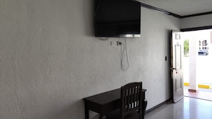 Quarto com televisão de tela plana na parede, uma mesa de madeira e uma cadeira.