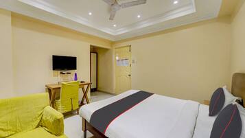 Quarto de hotel com cama, escrivaninha, cadeira, televisão e ventilador de teto.