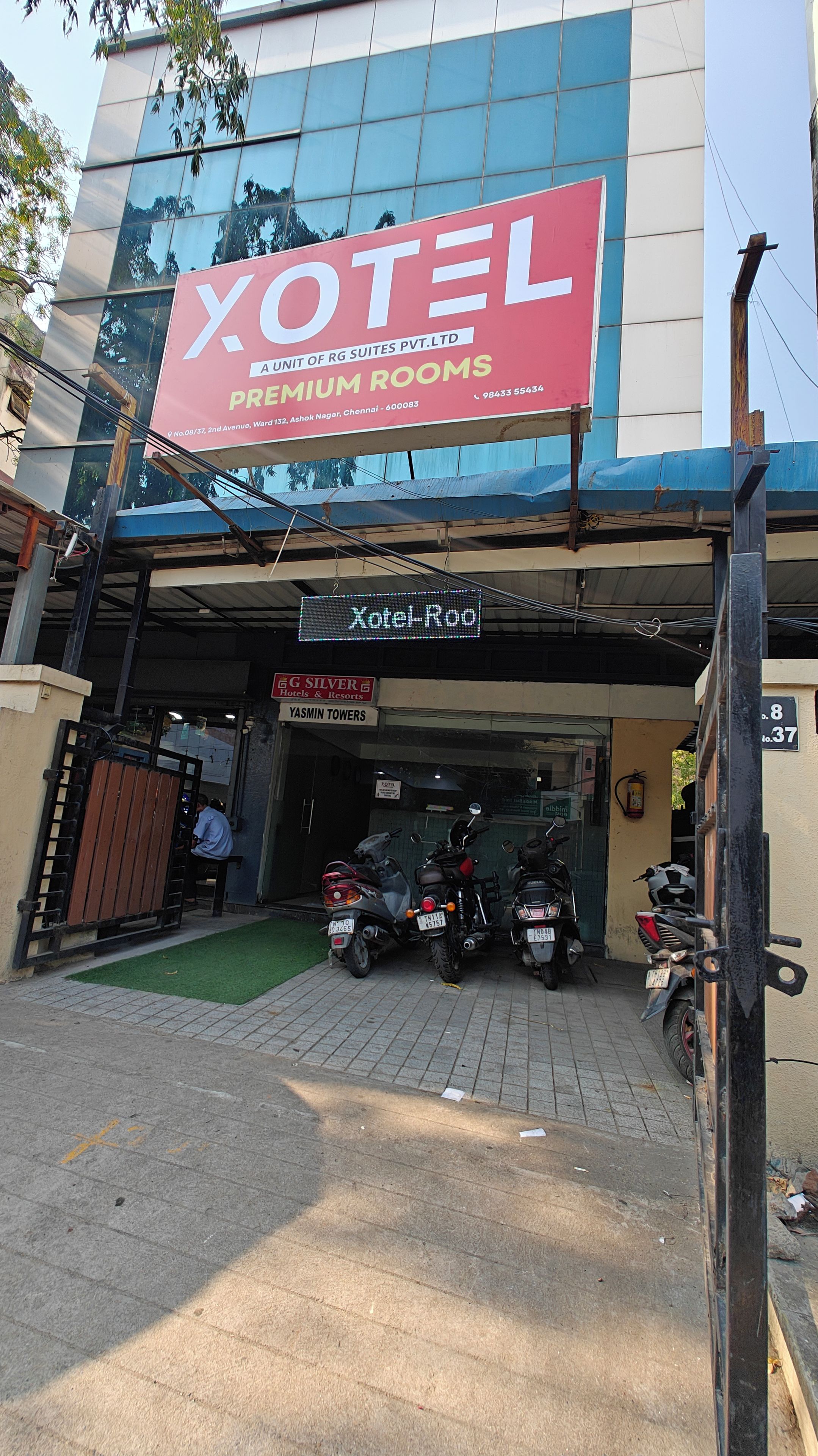 Um edifício com uma placa grande de 'XOTEL PREMIUM ROOMS', entrada por portão e várias motocicletas estacionadas.
