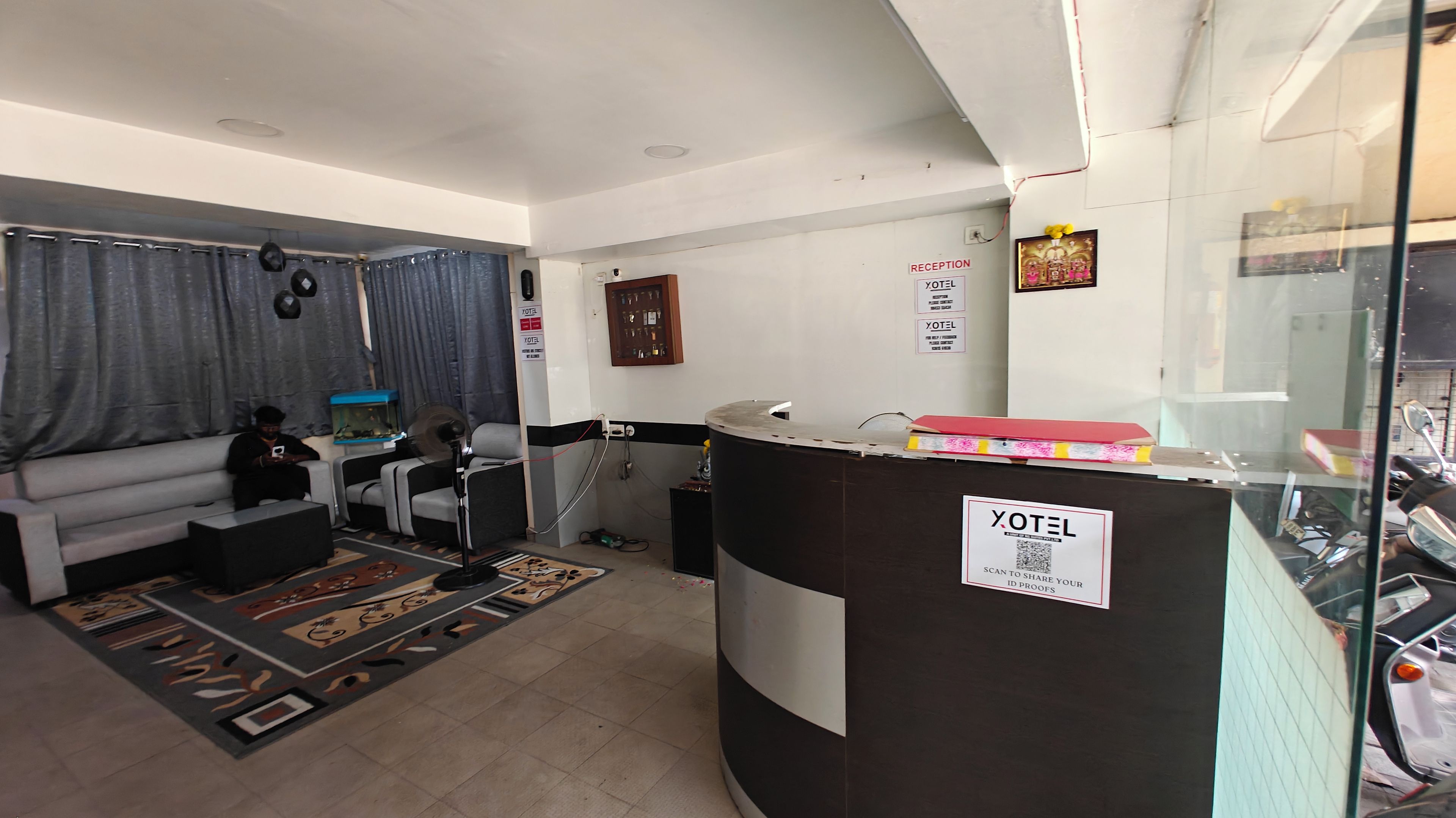 Bancada de recepção com placa indicando ser área de recepção de hotel, um aquário, um sofá e um ventilador no ambiente.