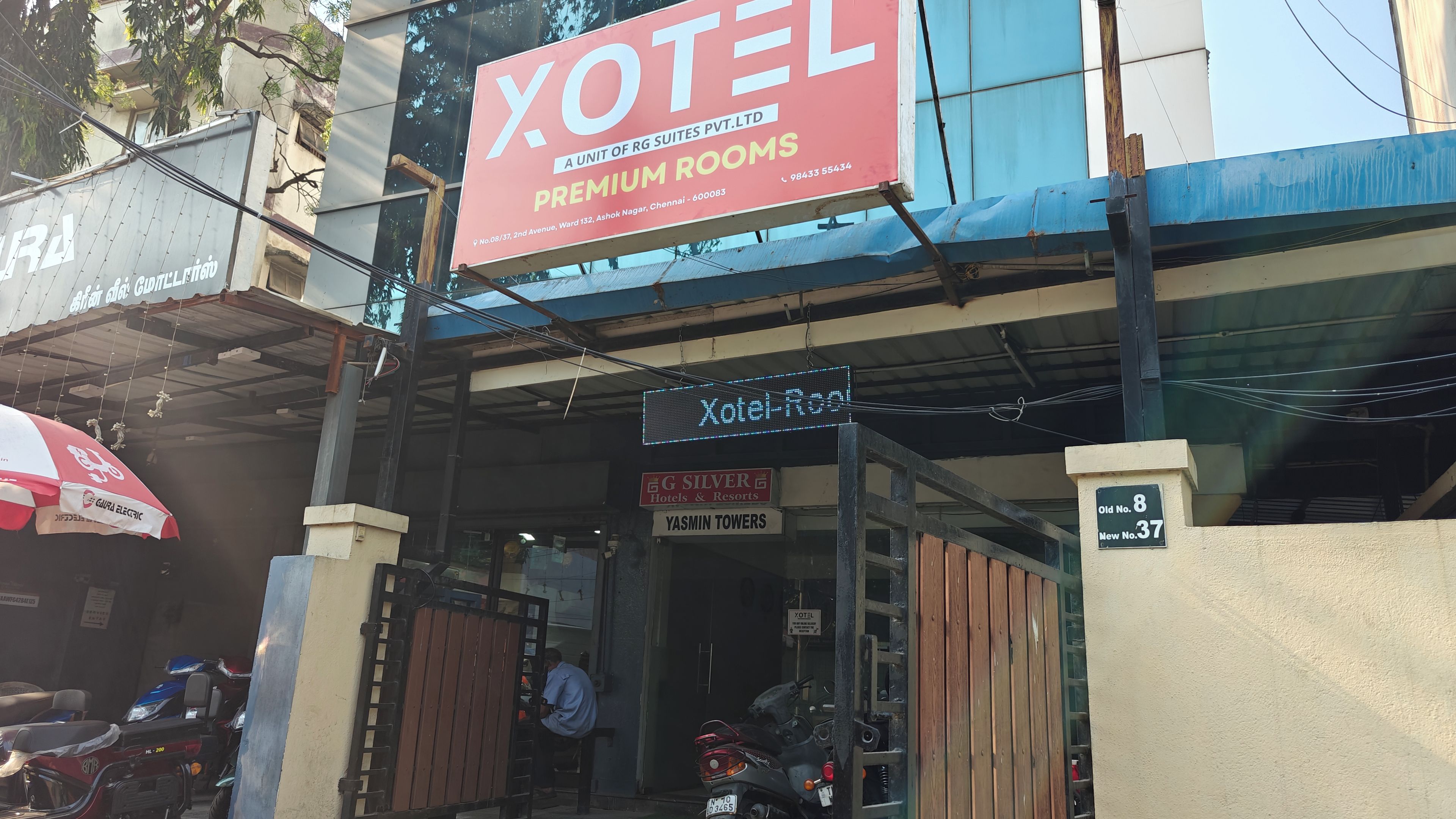 Hotel com placa chamativa anunciando quartos premium, painel de sinalização digital e entrada com portão.