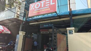 Hotel com placa chamativa anunciando quartos premium, painel de sinalização digital e entrada com portão.