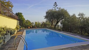 Piscina retangular com uma escada de metal de um lado, ladeada por um caminho de pedra e limitada por uma cerca de metal.