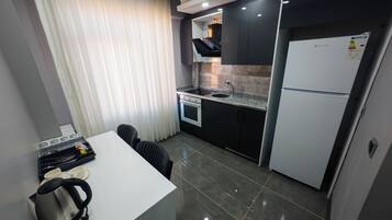 Cozinha compacta com bancada branca, armários pretos, forno embutido e geladeira.