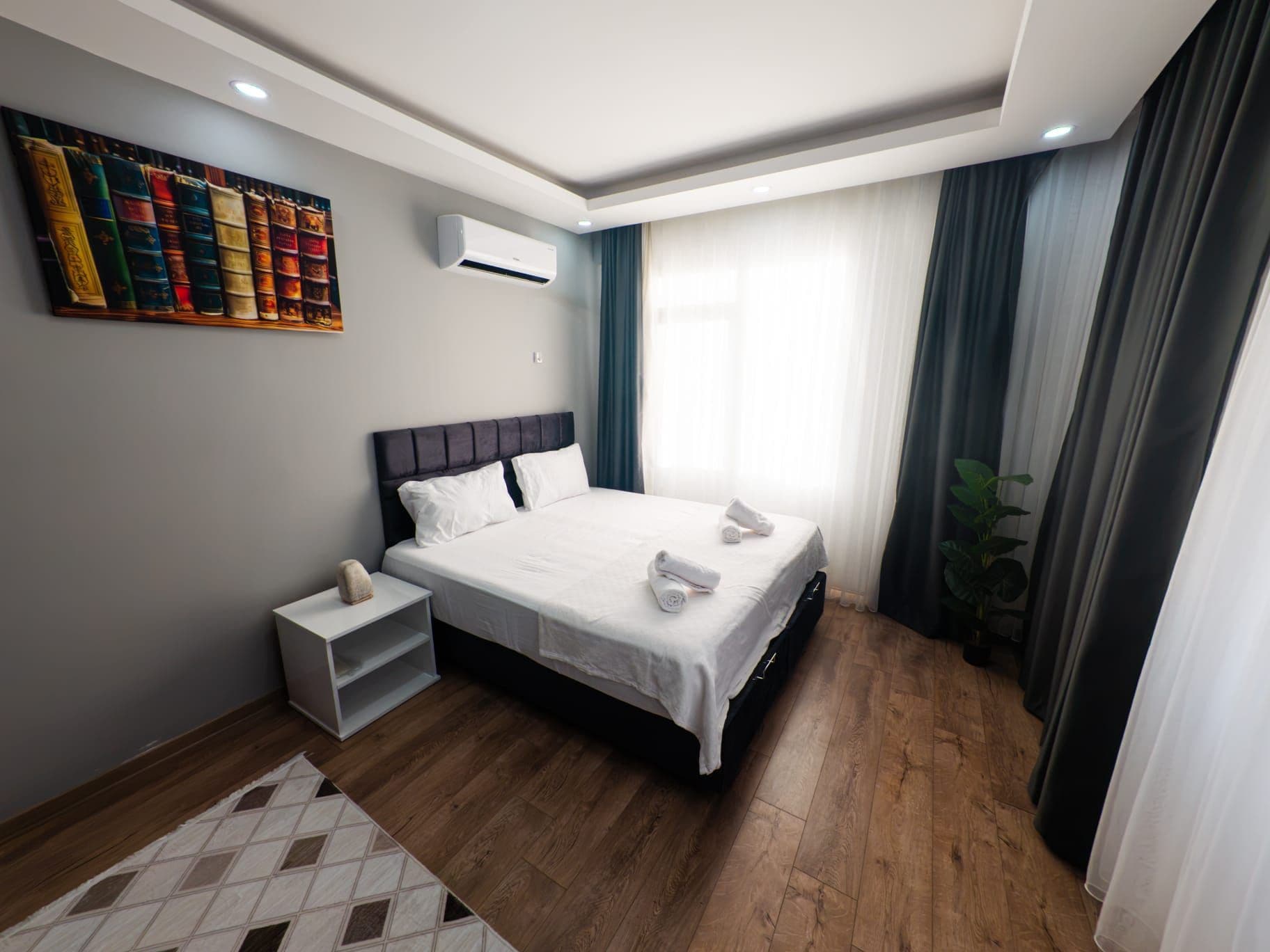 Quarto de hotel moderno com uma cama grande, mesa de cabeceira, ar condicionado fixado na parede e janela com cortinas.