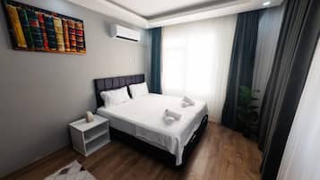 Quarto de hotel moderno com uma cama grande, mesa de cabeceira, ar condicionado fixado na parede e janela com cortinas.