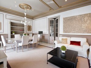 Ampla sala de estar com conjunto de jantar, sofá com almofadas decorativas e mesa de centro.