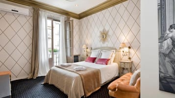 Quarto de hotel com uma cama, uma cadeira, uma mesinha de cabeceira e uma luminária na parede.