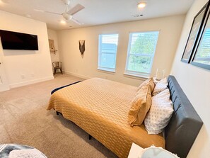 Quarto com cama, ventilador de teto, televisão de tela plana e duas janelas com persianas.