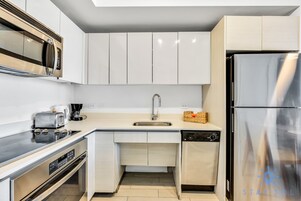 Cozinha compacta com micro-ondas, torradeira, cafeteira, pia, máquina de lavar louça e frigorífico.