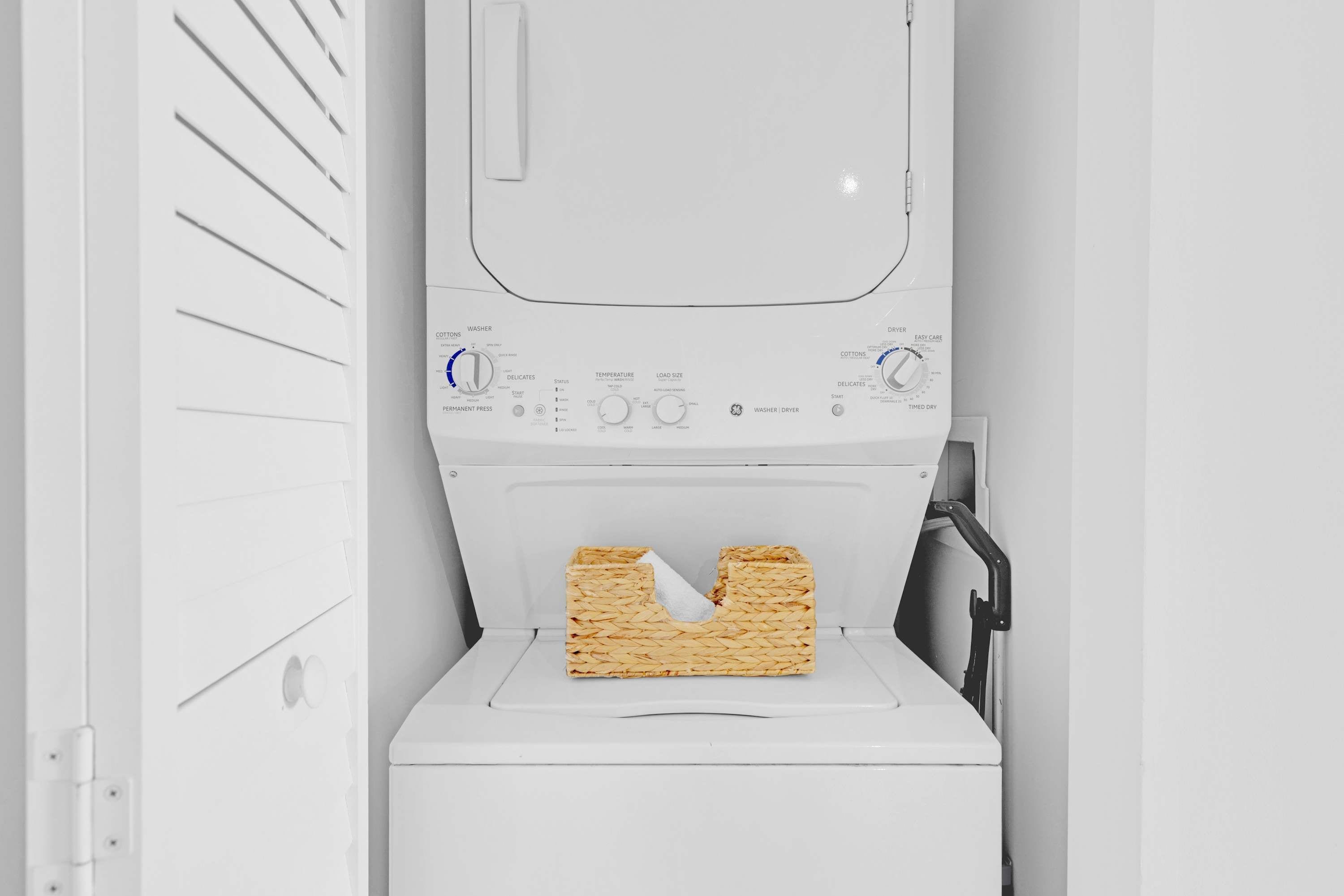 Vista frontal de uma máquina de lavar branca com painel de controle, uma cesta de vime e um cabo de alimentação.