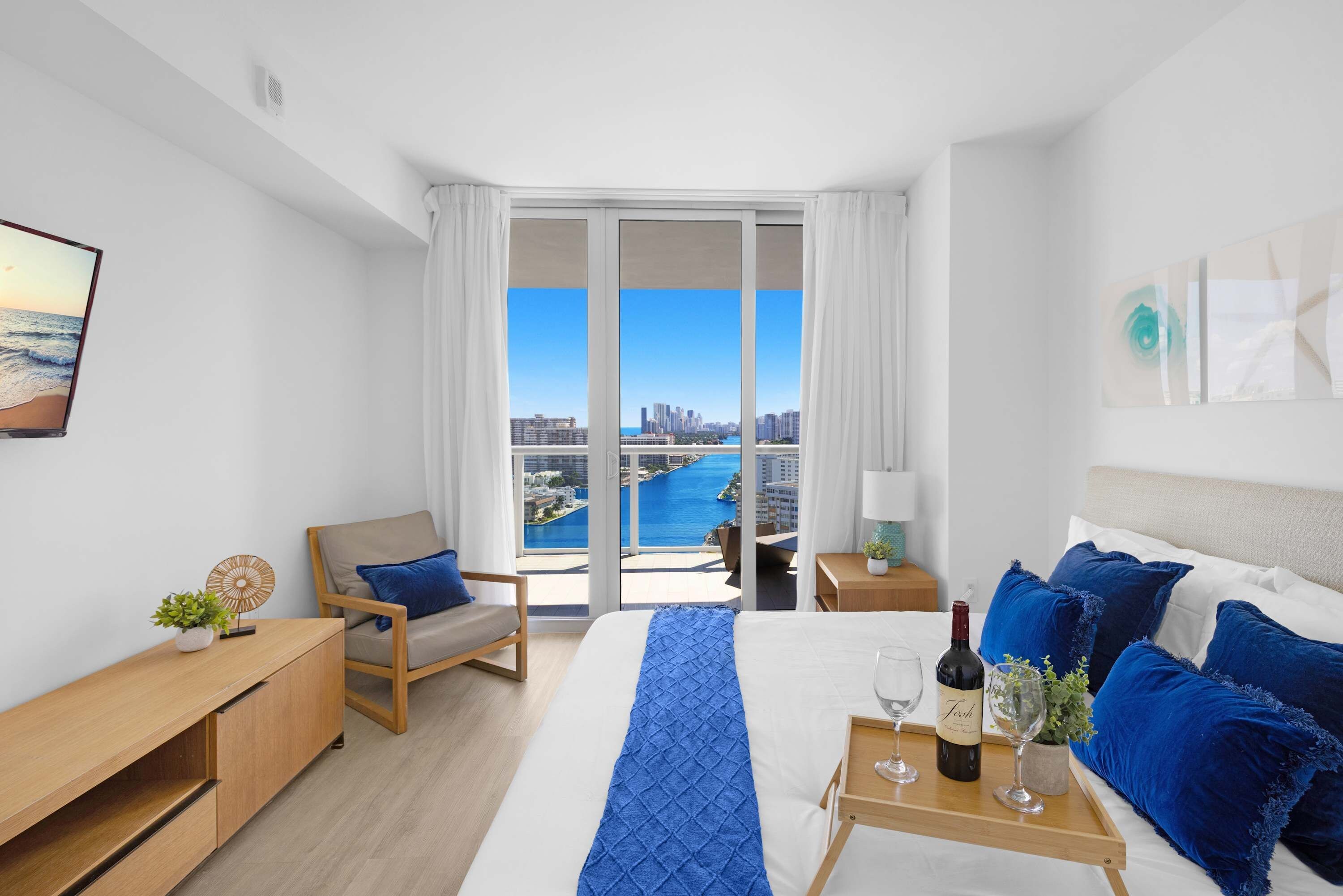 Quarto de hotel moderno com uma cama grande, uma escrivaninha, uma cadeira e vista para a cidade e para o mar pela varanda.