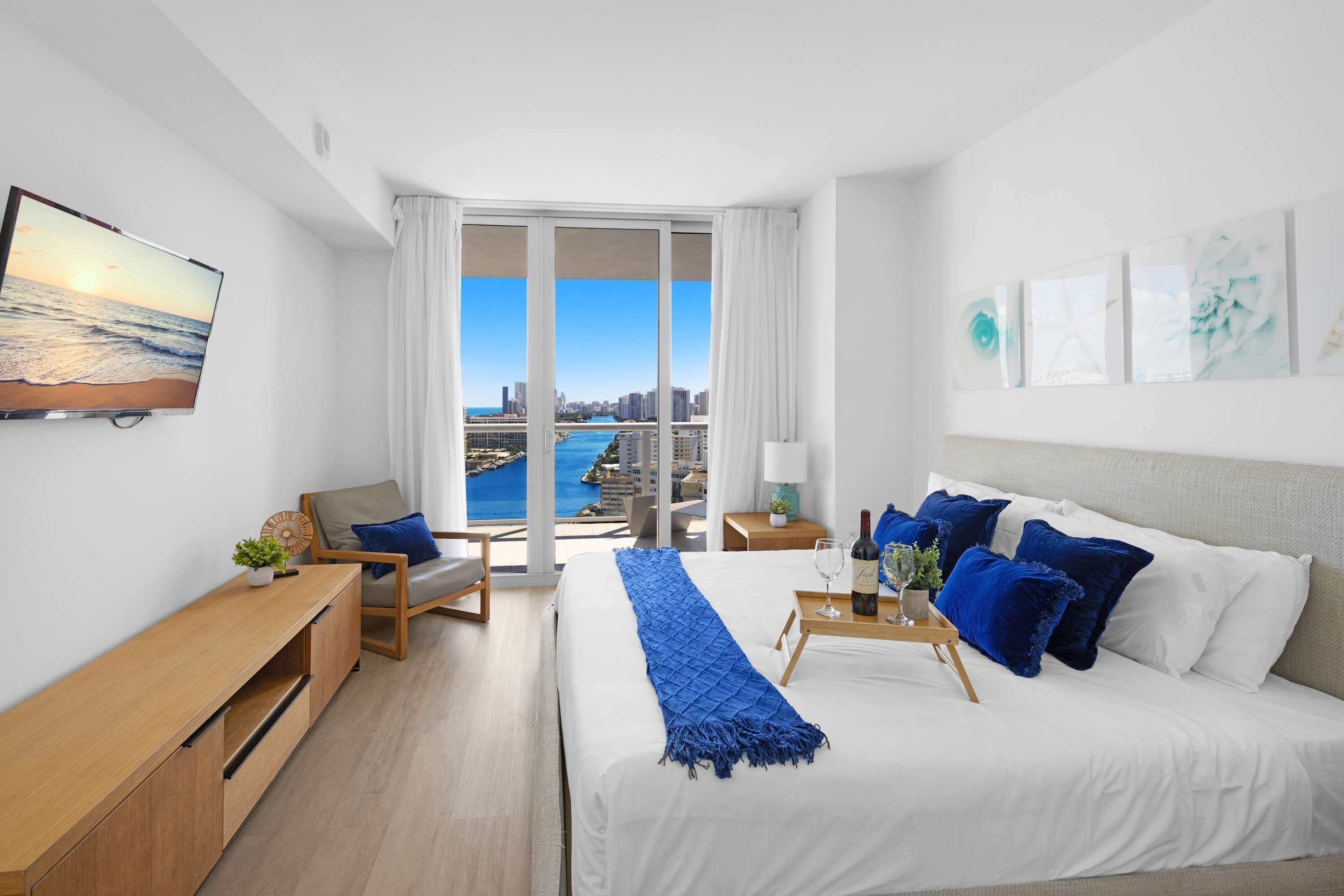 Quarto de hotel moderno com uma cama grande, uma escrivaninha, uma cadeira e vista para a cidade e para o mar.