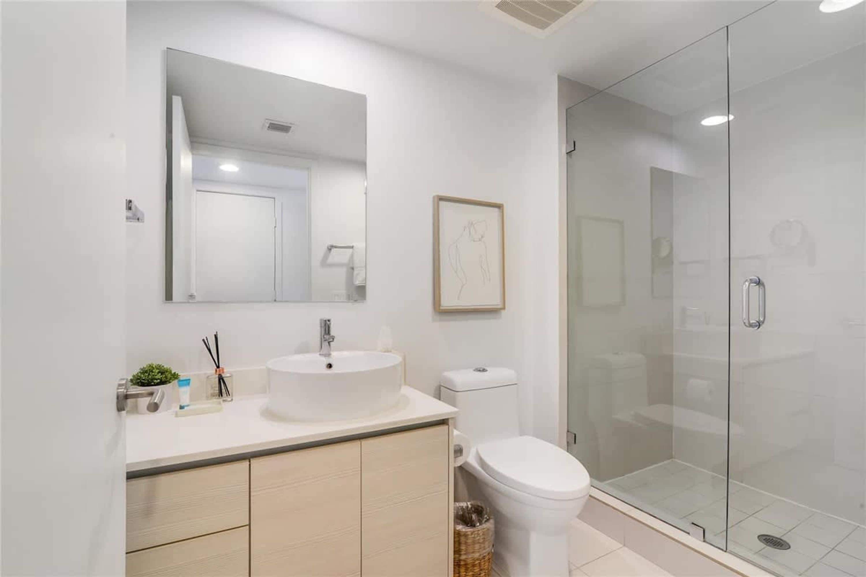 Um banheiro moderno com box de vidro, pia branca e vaso sanitário.