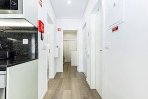 Corredor de hotel com área de cozinha à esquerda, um alarme de incêndio na parede e sinalização de saída de emergência.