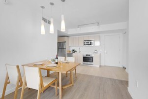 Cozinha moderna com eletrodomésticos de aço inoxidável, área de refeições com mesa e cadeiras de madeira e iluminação pendente.