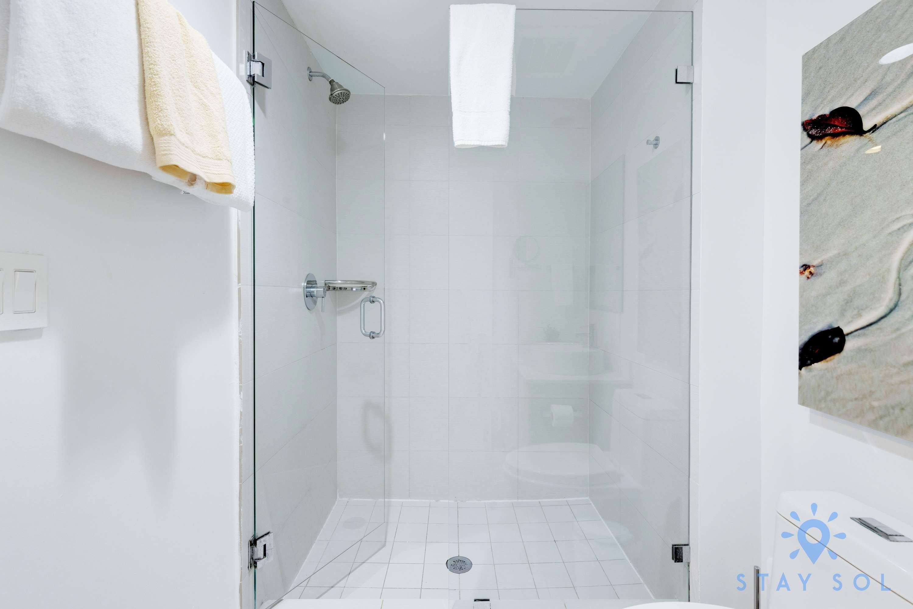Uma casa de banho moderna com porta de vidro, uma toalha branca pendurada na parede e ralo visível.