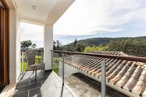 Varanda com vista para uma paisagem arborizada, uma cadeira e piso de azulejos.