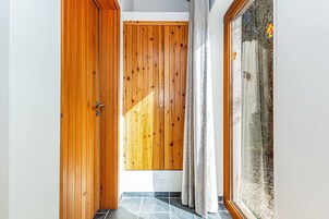 Uma porta de madeira com maçaneta de metal, uma janela com vista para árvores e um chão de azulejos.