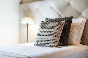 Cama bem arrumada com travesseiro listrado e manta de tricô escura.
