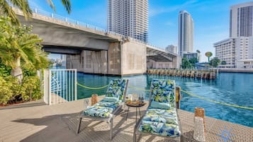 Um terraço à beira-mar com cadeiras de descanso e piscina, com vista para um horizonte urbano com edifícios altos.