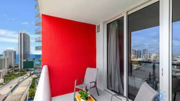 Varanda com parede vermelha, duas cadeiras, uma mesa pequena com uma planta e vista para a cidade.