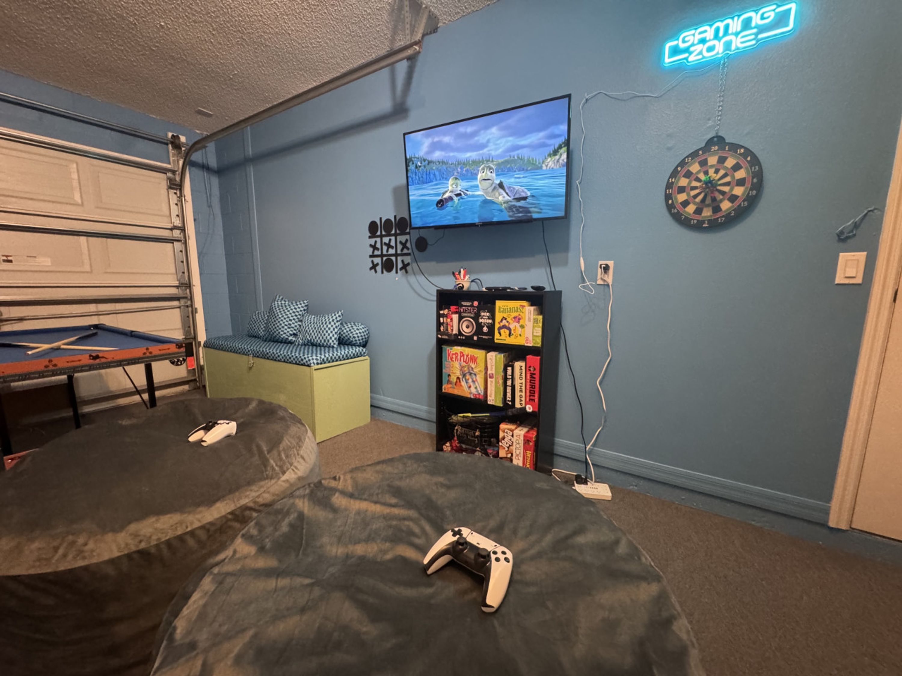 Um quarto com mesa de bilhar, área de jogos com dardos, televisão e estante com jogos de tabuleiro.