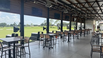 Área de estar interna com mesas e cadeiras, com vista para um campo de golfe.