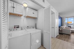 Uma lavanderia moderna com máquina de lavar e secar de carregamento frontal, um varal e uma luminária no teto.