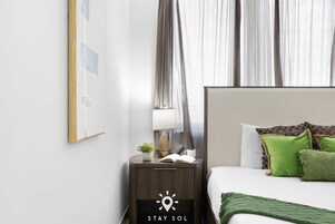 Quarto de hotel com cama, mesa de cabeceira, abajur e quadro na parede.
