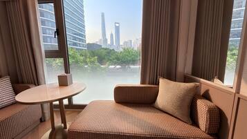 Quarto de hotel moderno com uma grande janela, um sofá, uma mesinha e vista para a paisagem urbana.