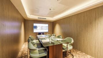 Sala de conferências com uma mesa grande, cadeiras, tela de projetor e parede de madeira.
