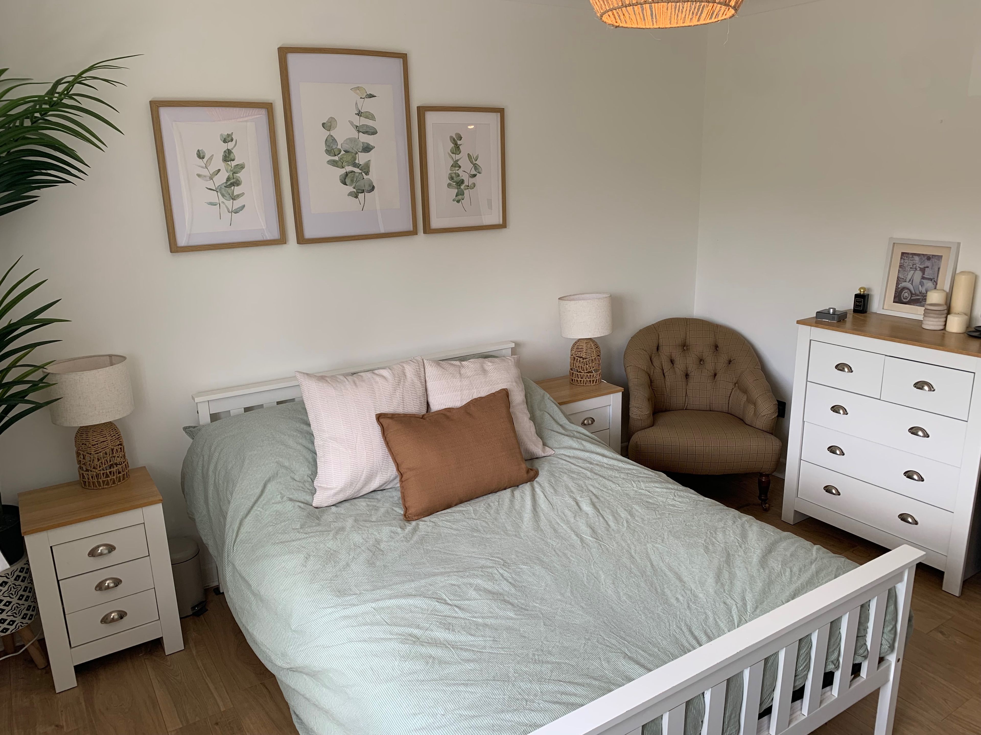 Quarto com cama, mesas de cabeceira, uma cadeira, cômoda e obra de arte na parede.