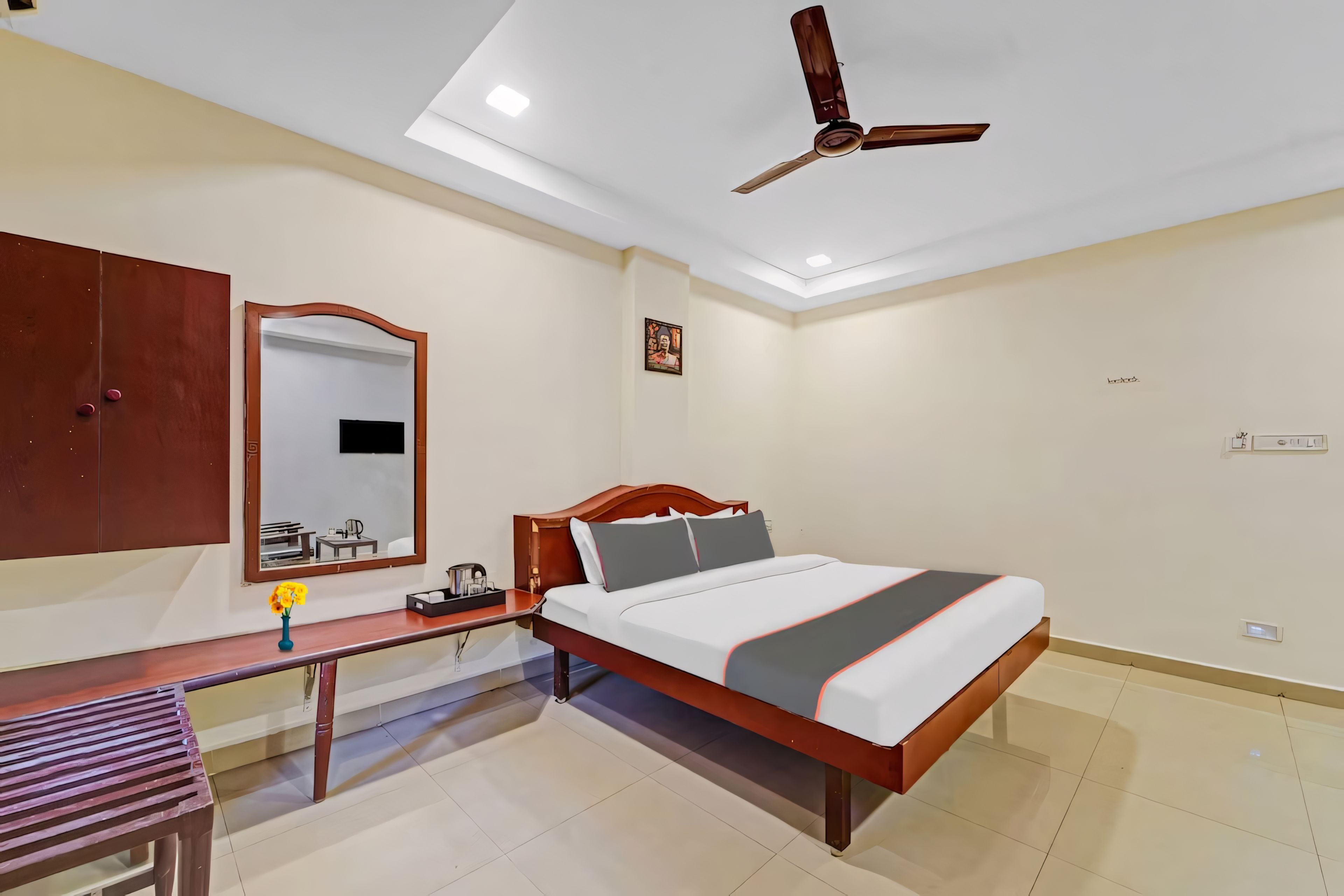 Quarto de hotel com cama, escrivaninha, guarda-roupa, ventoinha no teto e espelho.