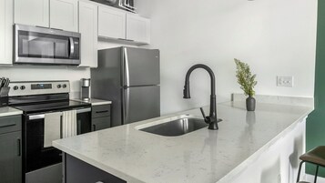 Uma cozinha moderna com eletrodomésticos de aço inoxidável, bancada de mármore e torneira preta.
