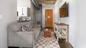 Um espaço de estar compacto com um sofá, uma mesa de madeira pequena e um tapete xadrez.