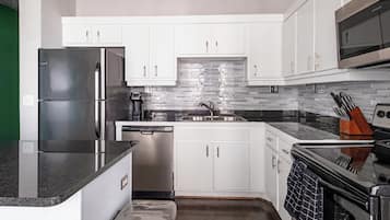 Cozinha moderna com armários brancos, eletrodomésticos de aço inoxidável e painel de azulejos.