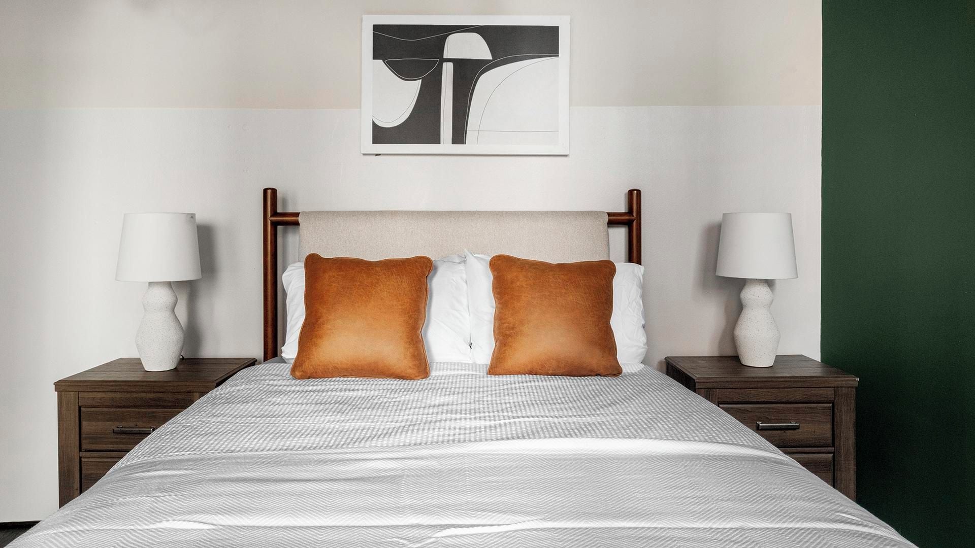 Quarto de hotel com cama, duas mesas de cabeceira e uma obra de arte abstrata pendurada na parede.