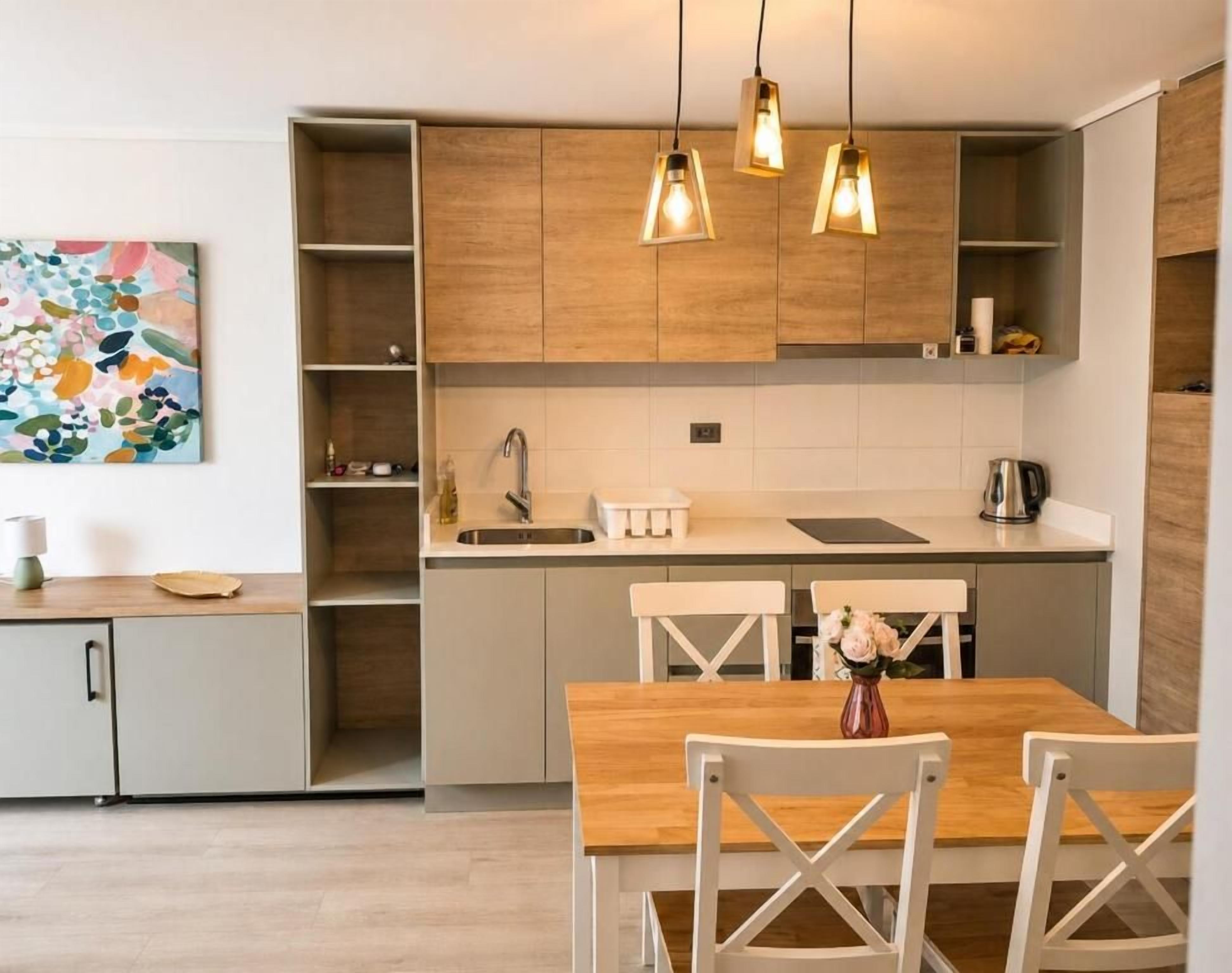 Cozinha moderna com armários de madeira, mesa de jantar com cadeiras e iluminação pendente.
