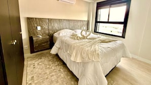 Quarto com cama, mesa de cabeceira, guarda-roupa, janela com persianas e tapete estampado.