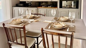 Uma sala de jantar com uma mesa posta para quatro pessoas, cadeiras de madeira e uma cozinha ao fundo.