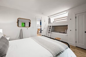Quarto com cama beliche, mesa de cabeceira, espelho e porta.