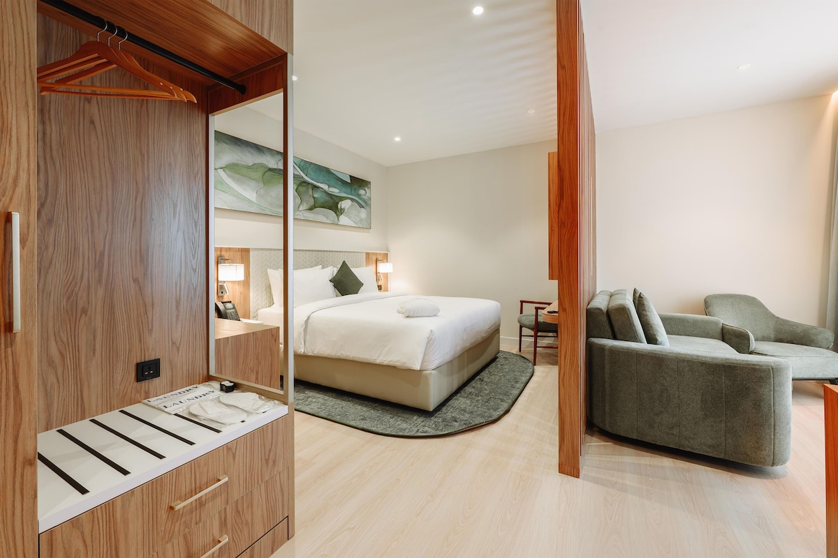 Quarto de hotel com cama, área de estar, guarda-roupa e espelho.
