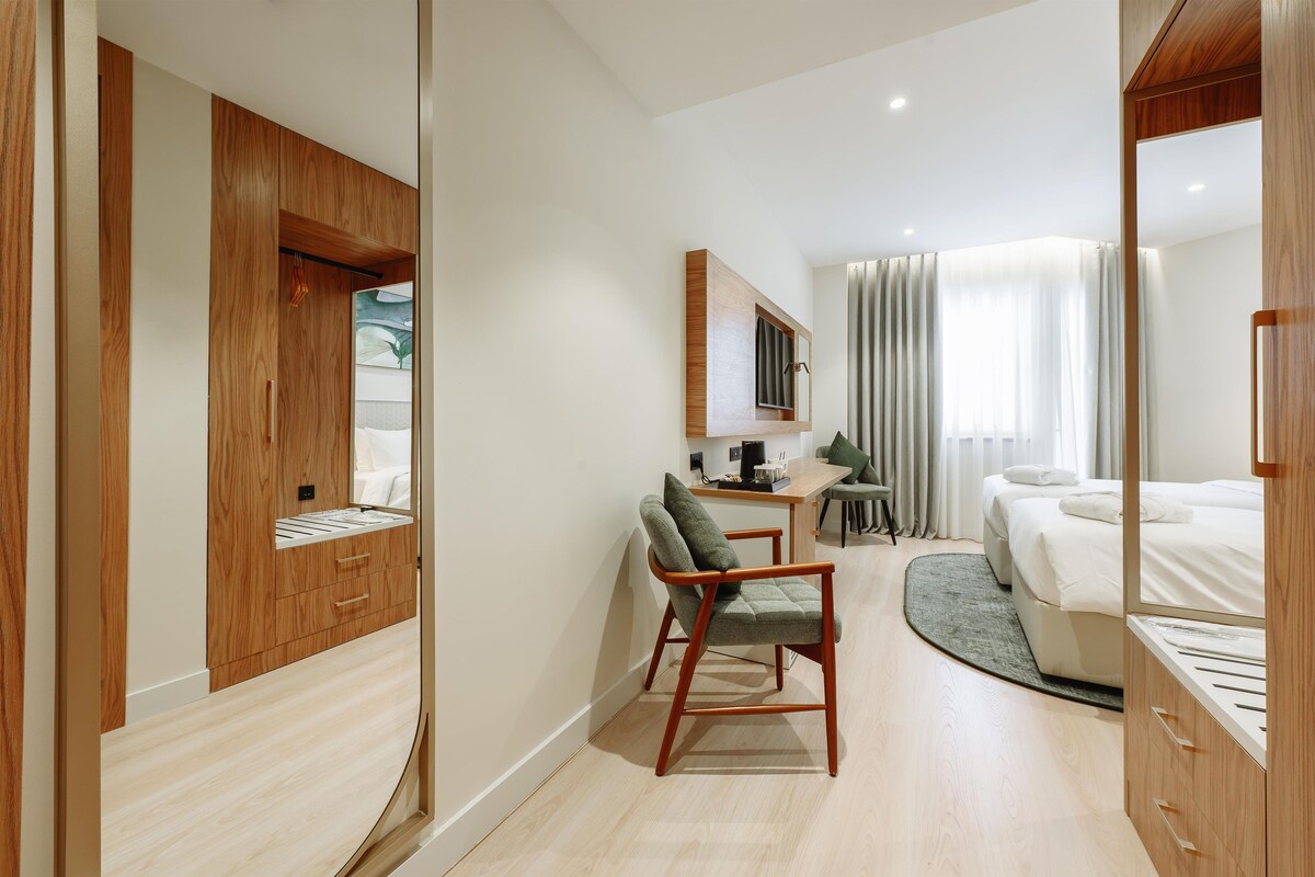 Quarto de hotel moderno com armário de madeira, escrivaninha com cadeira, cama e um espelho grande.