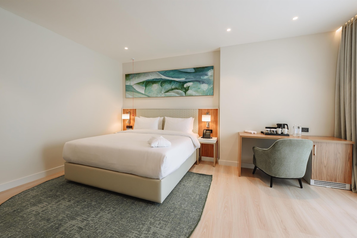 Quarto de hotel com cama grande, escrivaninha, cadeira, pintura na parede e telefone na escrivaninha.