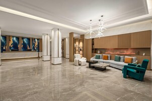 Um hall amplo com piso de mármore, área de estar com sofás e poltronas, lareira e balcão de recepção com painéis de vidro estampado.