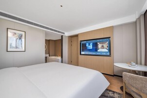 Quarto de hotel com uma cama grande, televisão presa à parede, uma mesa redonda pequena e uma cadeira.