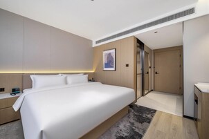 Quarto de hotel moderno com uma cama grande, mesas de cabeceira, guarda-roupa e banheiro com chuveiro e vaso sanitário.