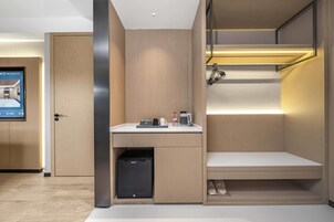 Quarto de hotel moderno com escrivaninha embutida, um cantinho de estar e uma televisão exibindo informações do quarto.